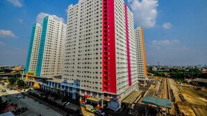 Um edifício com várias andares e uma faixa vermelha vertical marcante, situado numa área urbana movimentada com ruas e veículos.