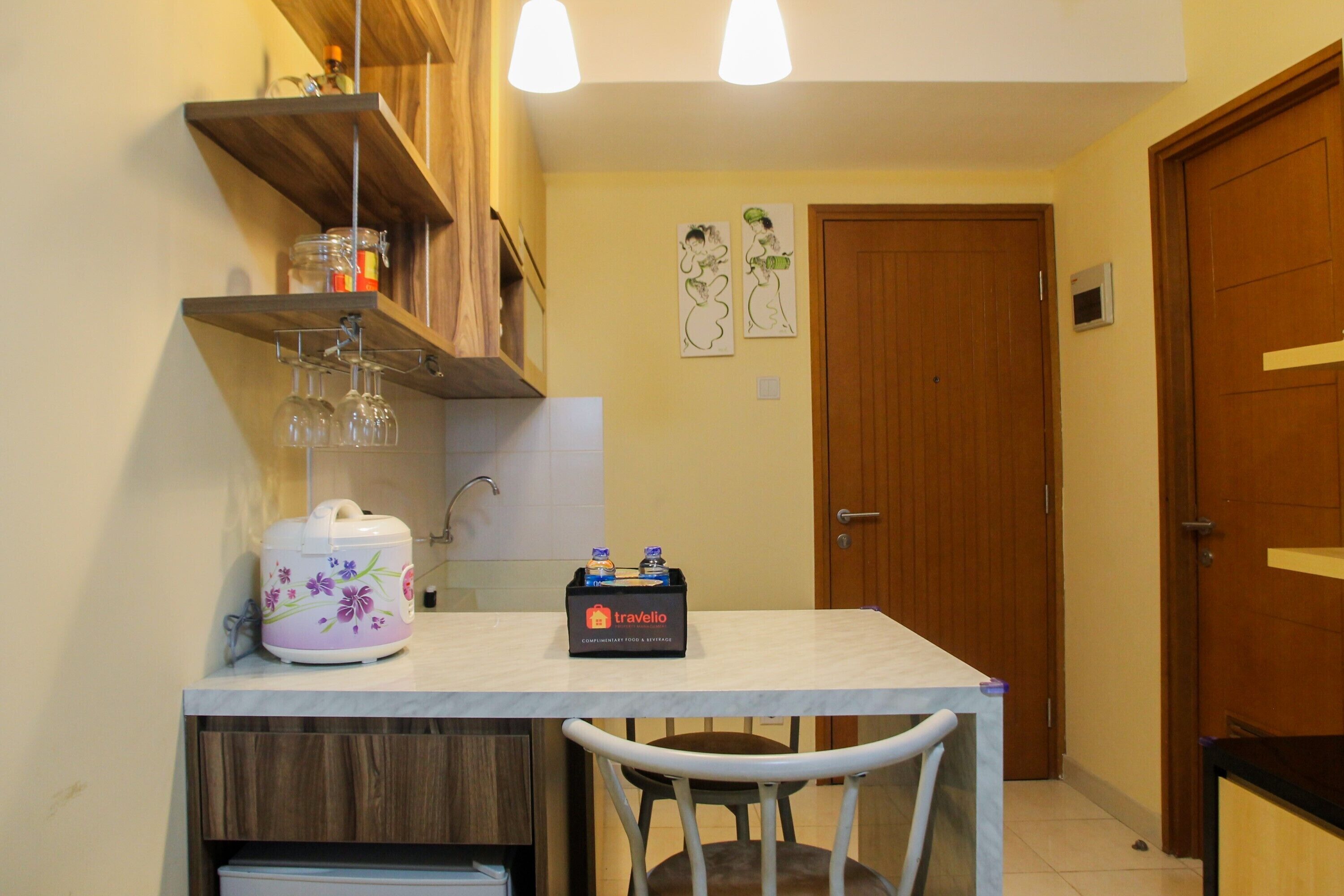 Uma cozinha compacta com bancada, pia e armário. Uma cadeira e uma porta aparecem ao fundo.