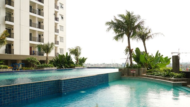 Piscina com bordas azulejadas, rodeada por vegetação e um edifício alto ao fundo.