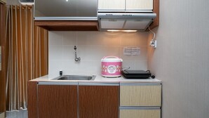 Uma cozinha compacta com pia, panela de arroz e chaleira elétrica preta no balcão.