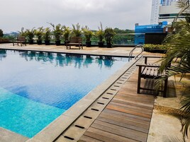 Piscina com deck de madeira e plantas em vasos, cercada por edifícios.