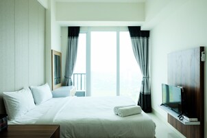 Quarto de hotel com uma cama grande, televisão fixada na parede e varanda com cortinas.