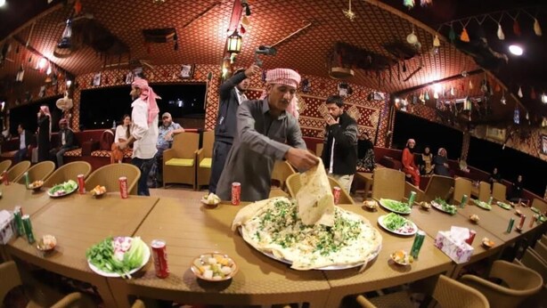 Restaurante com uma grande mesa redonda posta para refeição, rodeada por cadeiras de vime.