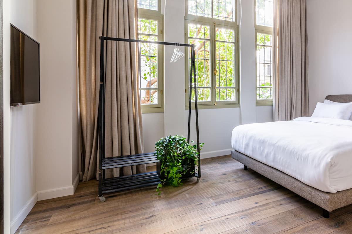 Quarto com cama, televisão, janela com cortinas e uma planta.
