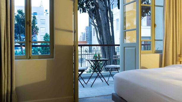 Quarto de hotel com varanda, cama e mesa com duas cadeiras.