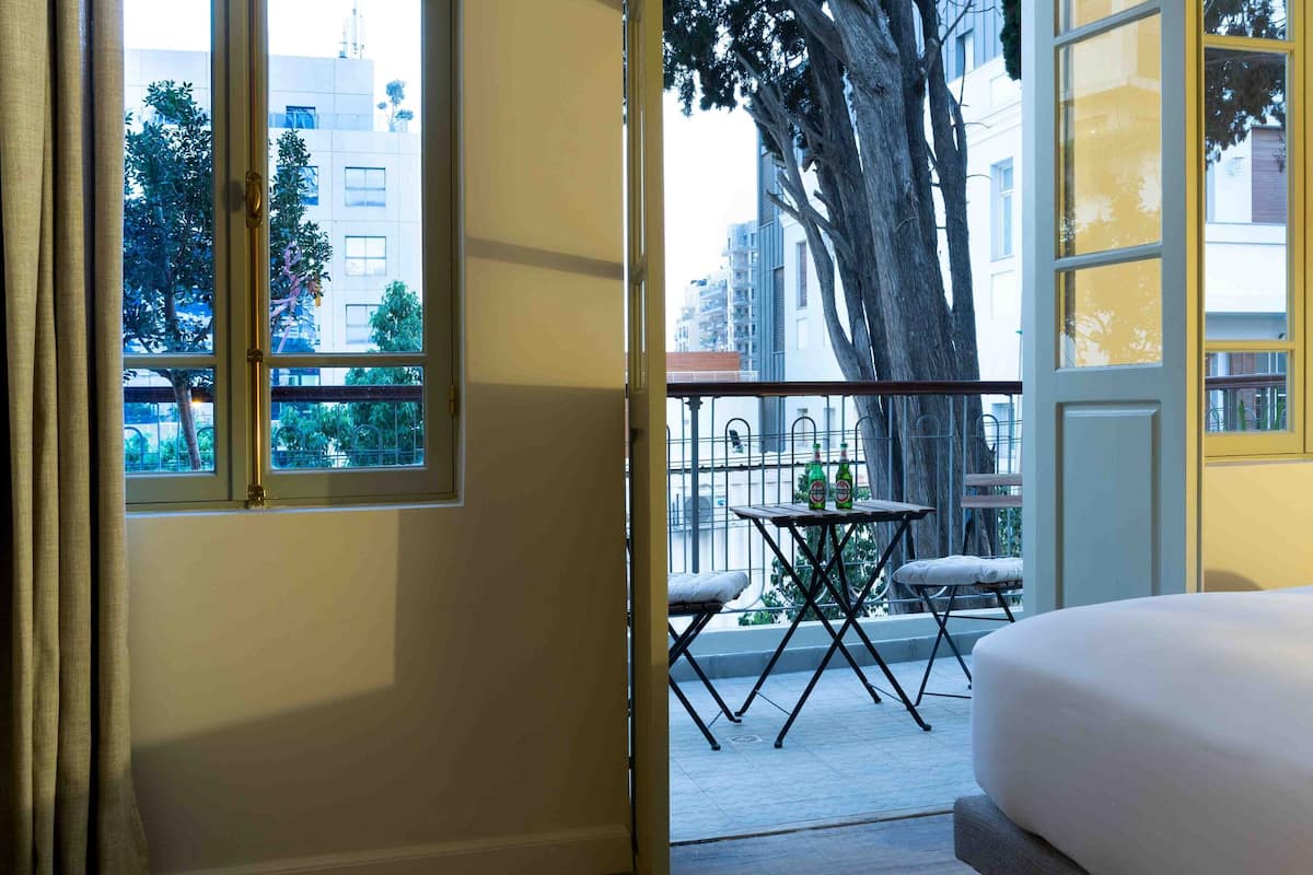 Quarto de hotel com varanda, cama e mesa com duas cadeiras.