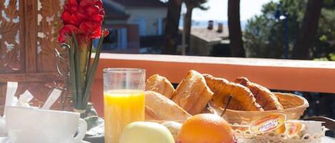 Bandeja de café da manhã com croissants, um copo de suco de laranja, uma xícara e um vaso de flores vermelhas.