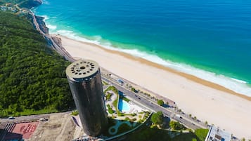 Vista aérea de uma área costeira com um prédio alto, uma praia e uma estrada.