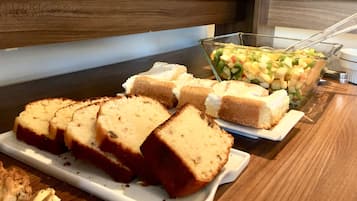 Um buffet de café da manhã com pão fatiado e salada de frutas.