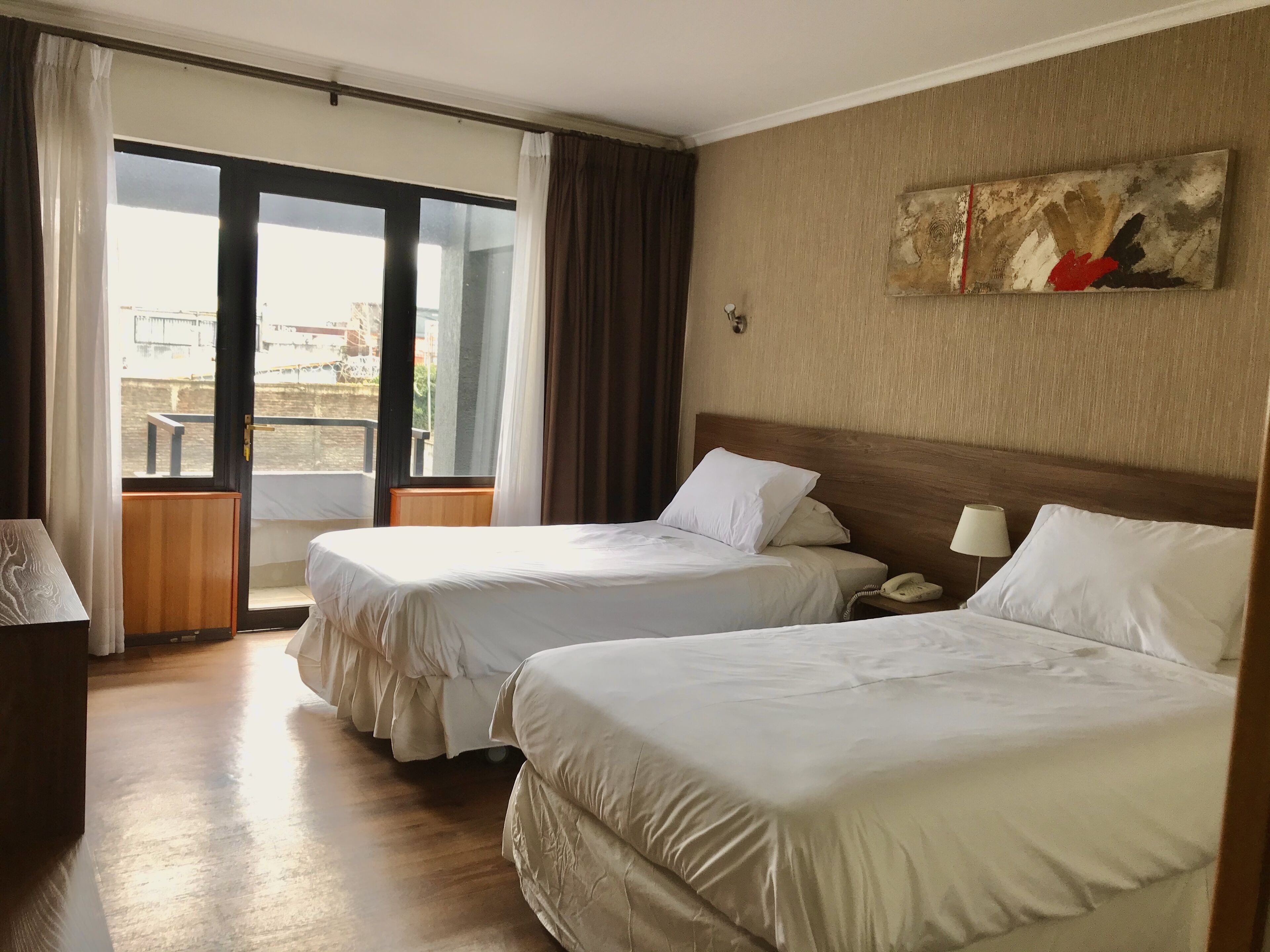 Quarto de hotel com duas camas, uma varanda, um quadro na parede e um telefone na mesa de cabeceira.