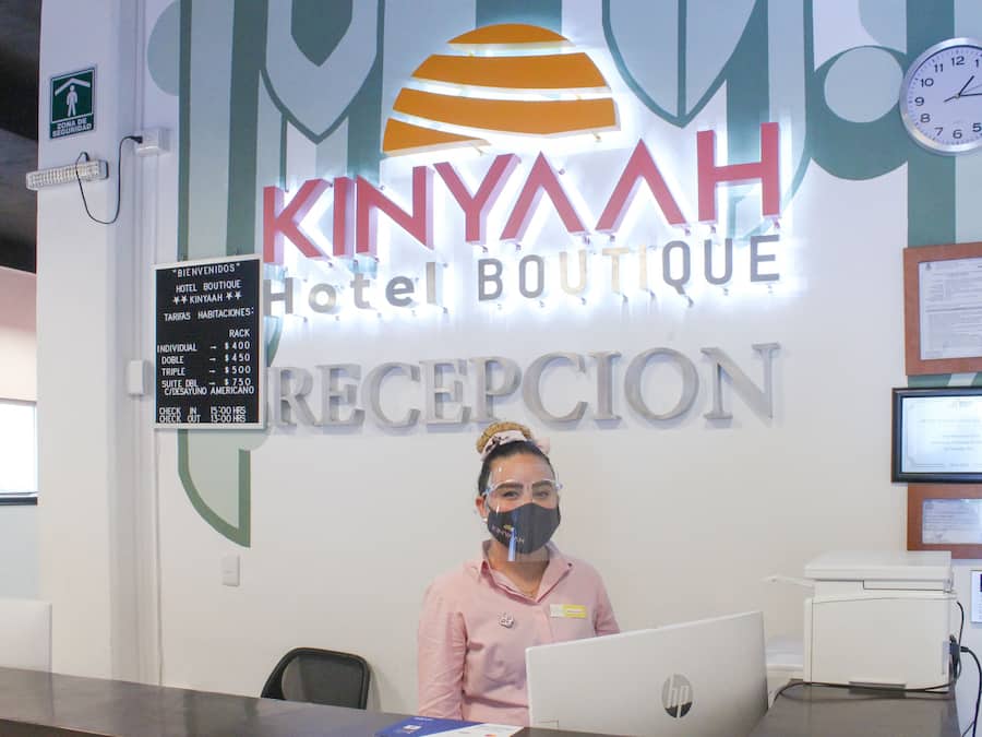 Bancada de recepção no Kinyaah Hotel Boutique com um aviso indicando tarifas de quarto e um relógio.