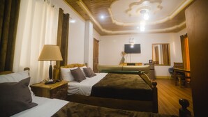 Quarto de hotel com teto de madeira, cama com cabeceira, mesa de cabeceira com abajur, cômoda, escrivaninha com cadeira e espelho.