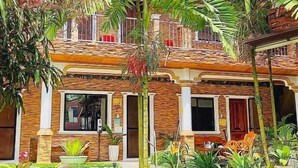 Edifício de dois andares com fachada de madeira e várias janelas. Há plantas em vasos e uma pequena área de estar ao ar livre na frente.
