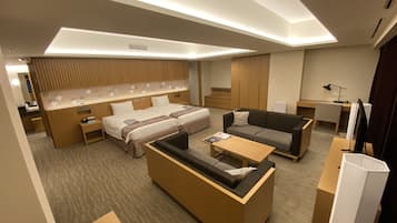 Quarto de hotel moderno com sofá, duas camas, escrivaninha e televisão de tela plana.