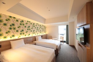 Quarto de hotel com duas camas, uma televisão, uma mesa pequena e uma janela com vista.