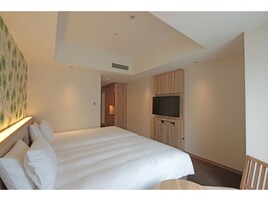 Quarto de hotel com uma cama grande, televisão de tela plana, armários de madeira e uma porta que dá para outro quarto.