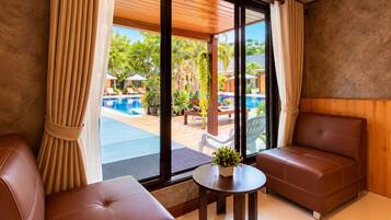 Quarto com vista para piscina ao ar livre, sofá, mesa com planta e janela com cortinas.