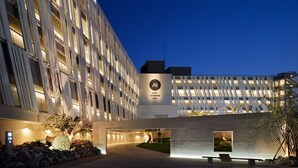 Um hotel moderno com um logotipo 'AR' em destaque, uma área externa coberta e uma placa de limite de altura.