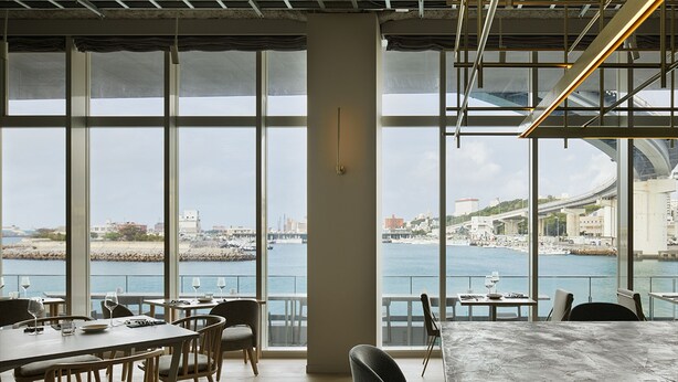 Uma área de refeições moderna com grandes janelas com vista para o horizonte urbano à beira-mar.