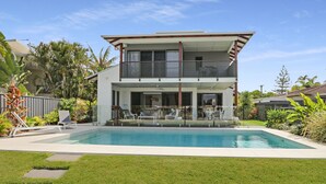 Uma casa de dois andares com piscina, área de estar externa e vegetação exuberante.