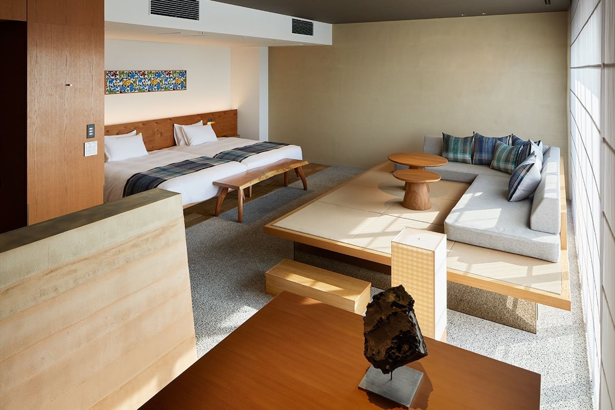 Quarto de hotel moderno com cama, sofá e uma pequena mesa com uma escultura.