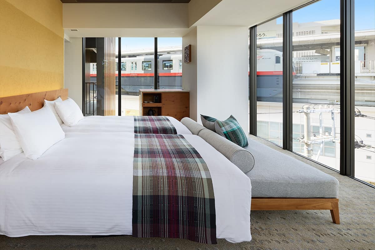 Quarto de hotel moderno com uma cama grande, um sofá e vista para um trem pela janela.