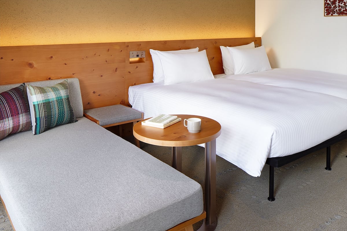 Quarto de hotel com cama, sofá, mesinha e criado-mudo.