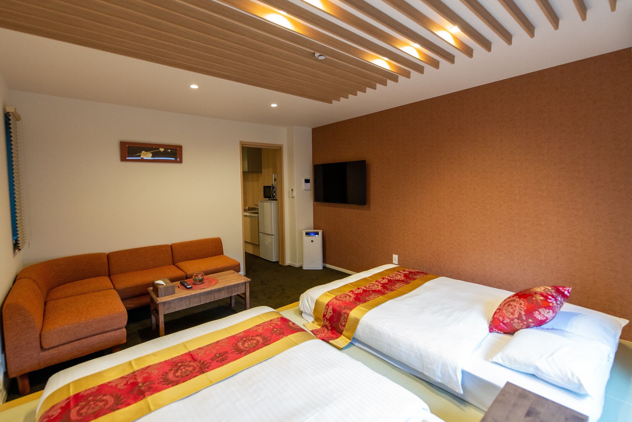 Quarto de hotel com duas camas, um sofá, uma mesinha, uma televisão e um micro-ondas.
