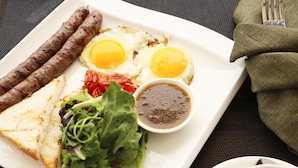 Prato de café da manhã com salsichas, ovos, torradas, salada e uma pequena tigela de molho.
