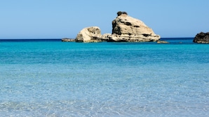 Mar azul transparente com um afloramento rochoso ao longe.