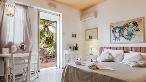 Quarto de hotel com cama, secretária, cadeira, mesa e vista para um jardim.
