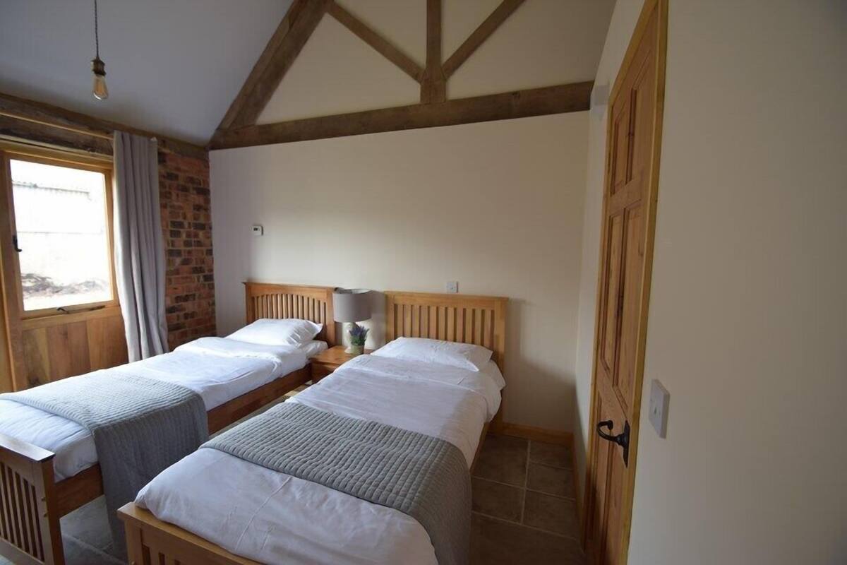 Quarto com duas camas de madeira, parede de tijolos e porta de madeira.