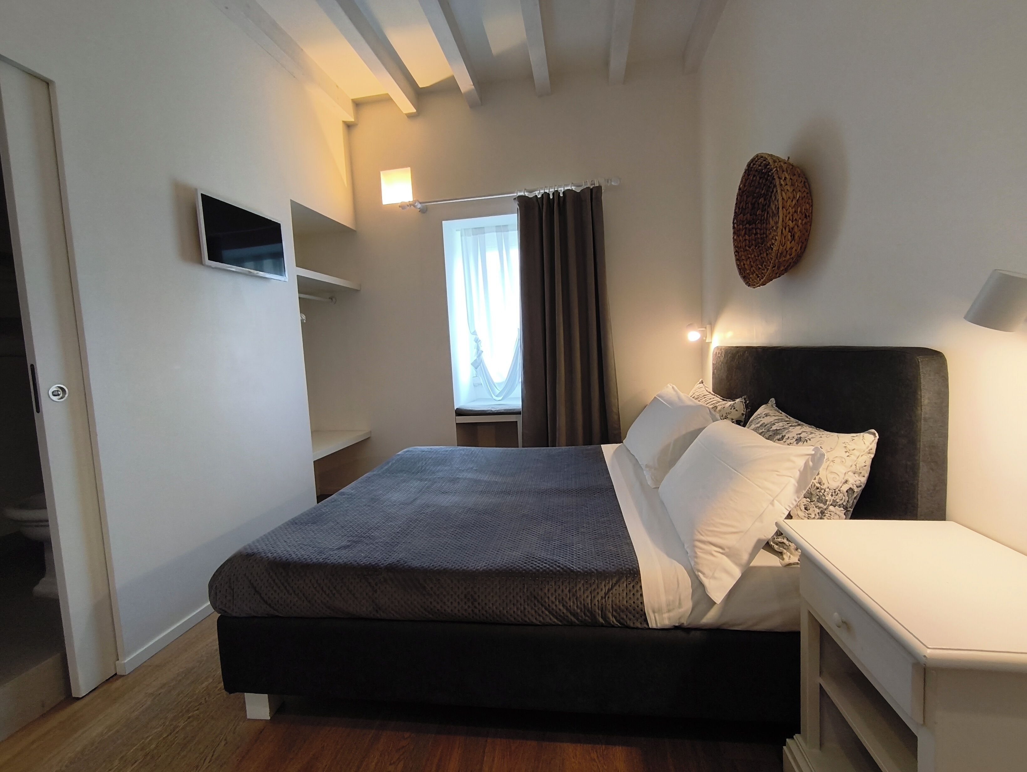 Quarto com cama, mesa de cabeceira e janela com cortinas.