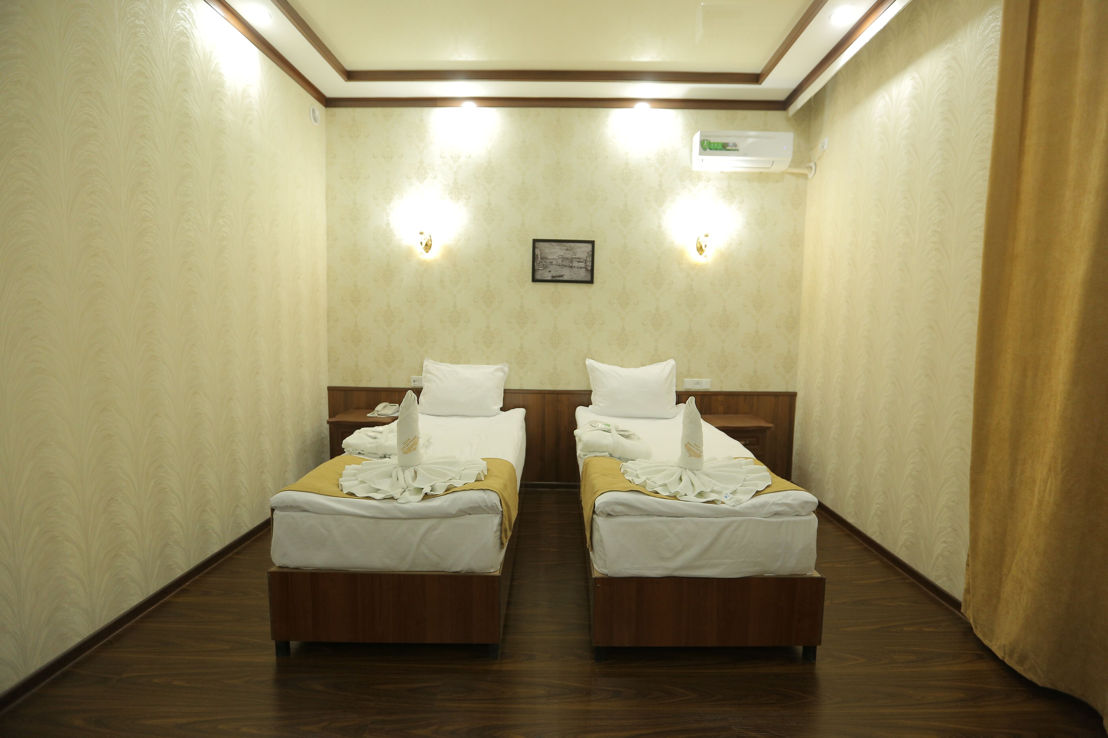 Quarto de hotel com duas camas de solteiro, cabeceiras de madeira, pequenas mesas de cabeceira e um quadro emoldurado na parede.