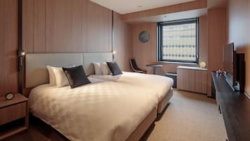 Quarto de hotel moderno com uma cama grande, uma escrivaninha, uma cadeira e uma televisão.