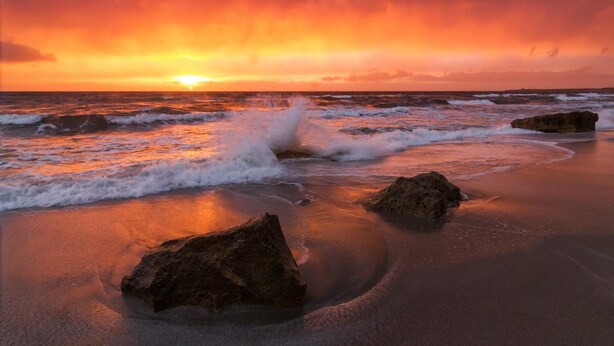 Uma praia com rochas e ondas ao pôr do sol.