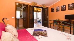 Quarto com sofá rosa, mesa de jantar com cadeiras, televisão e estante de livros.