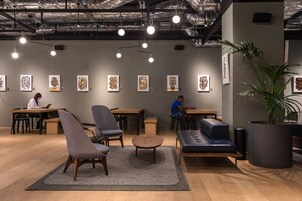 Um interior moderno com piso de madeira, um sofá cinza, uma mesa de centro redonda e uma grande planta em vaso.