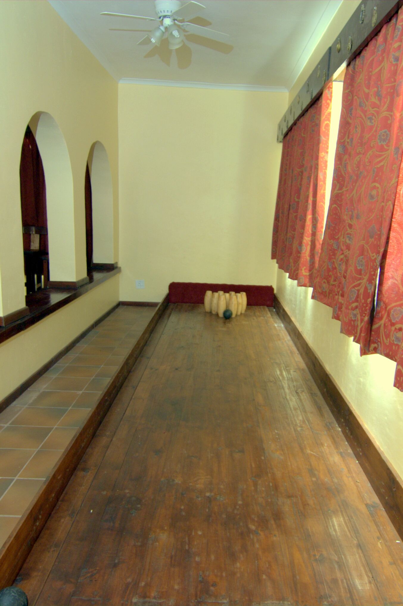 Quarto com piso de madeira, ventilador de teto, cortinas vermelhas e parede revestida de azulejos.
