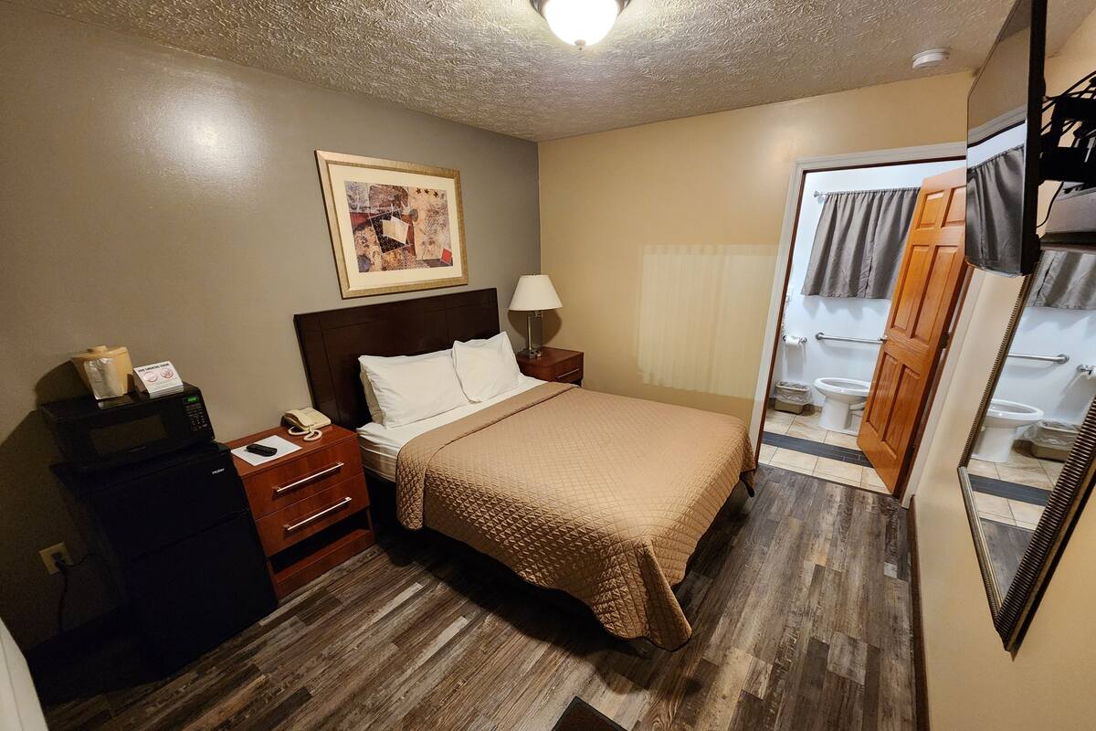Quarto de hotel com uma cama, uma escrivaninha com telefone, micro-ondas e um quadro na parede.
