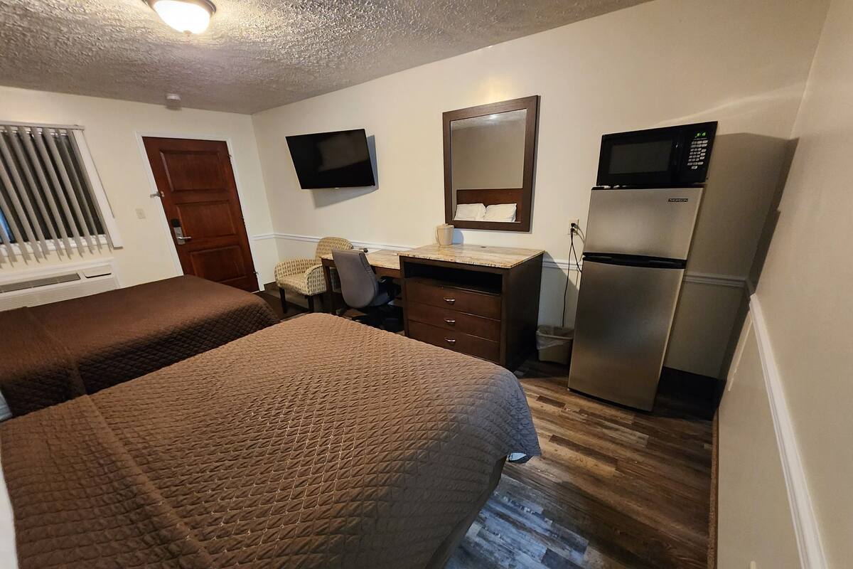 Quarto de hotel com duas camas, uma escrivaninha, uma cadeira, uma TV, micro-ondas e frigorífico.