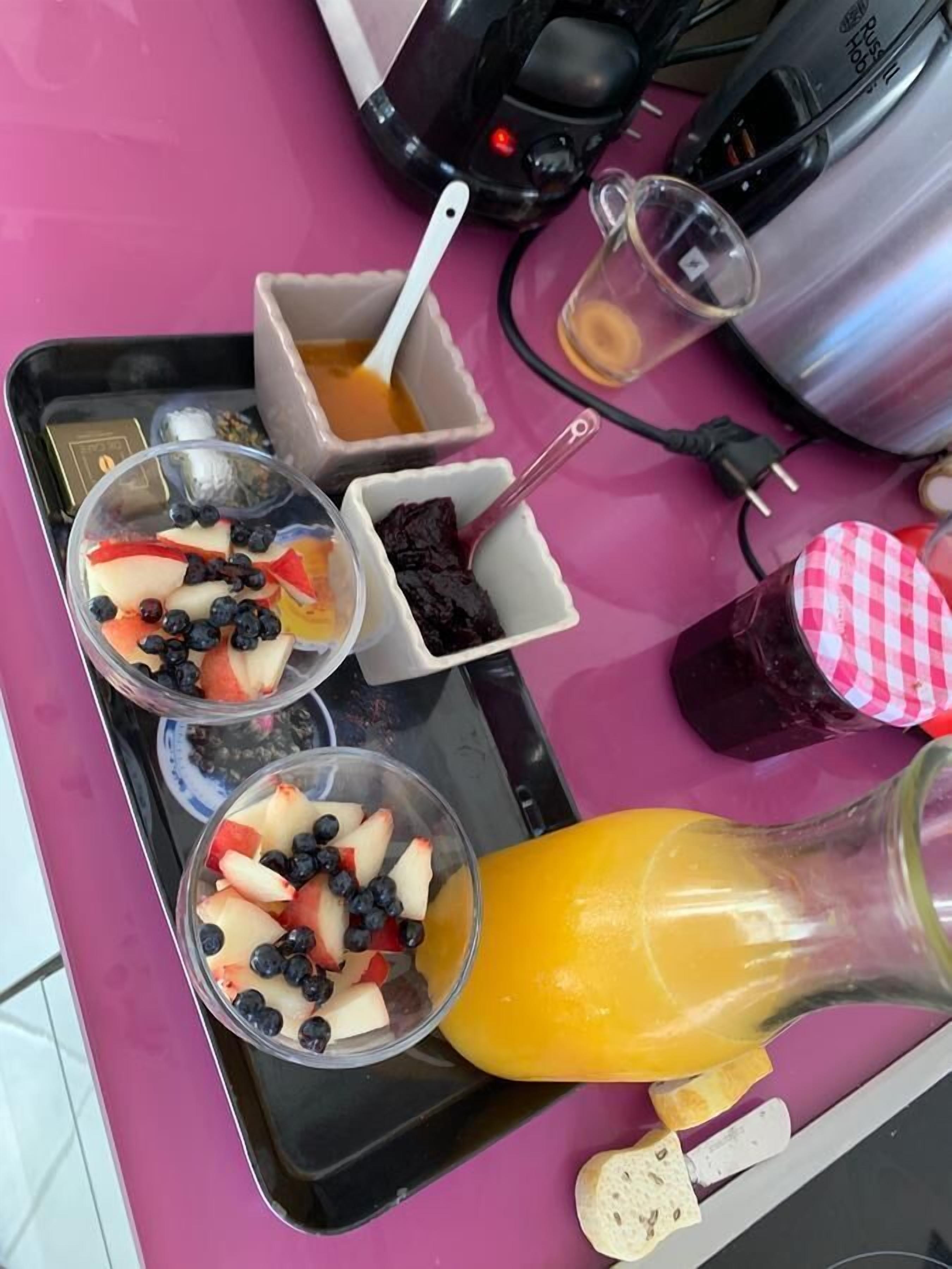 Uma bandeja com três copos de vidro contendo frutas e uma garrafa de suco de laranja.