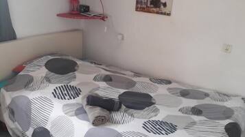 Um quarto com uma cama, uma televisão sobre um suporte, e uma parede com quadros e um abajur vermelho.