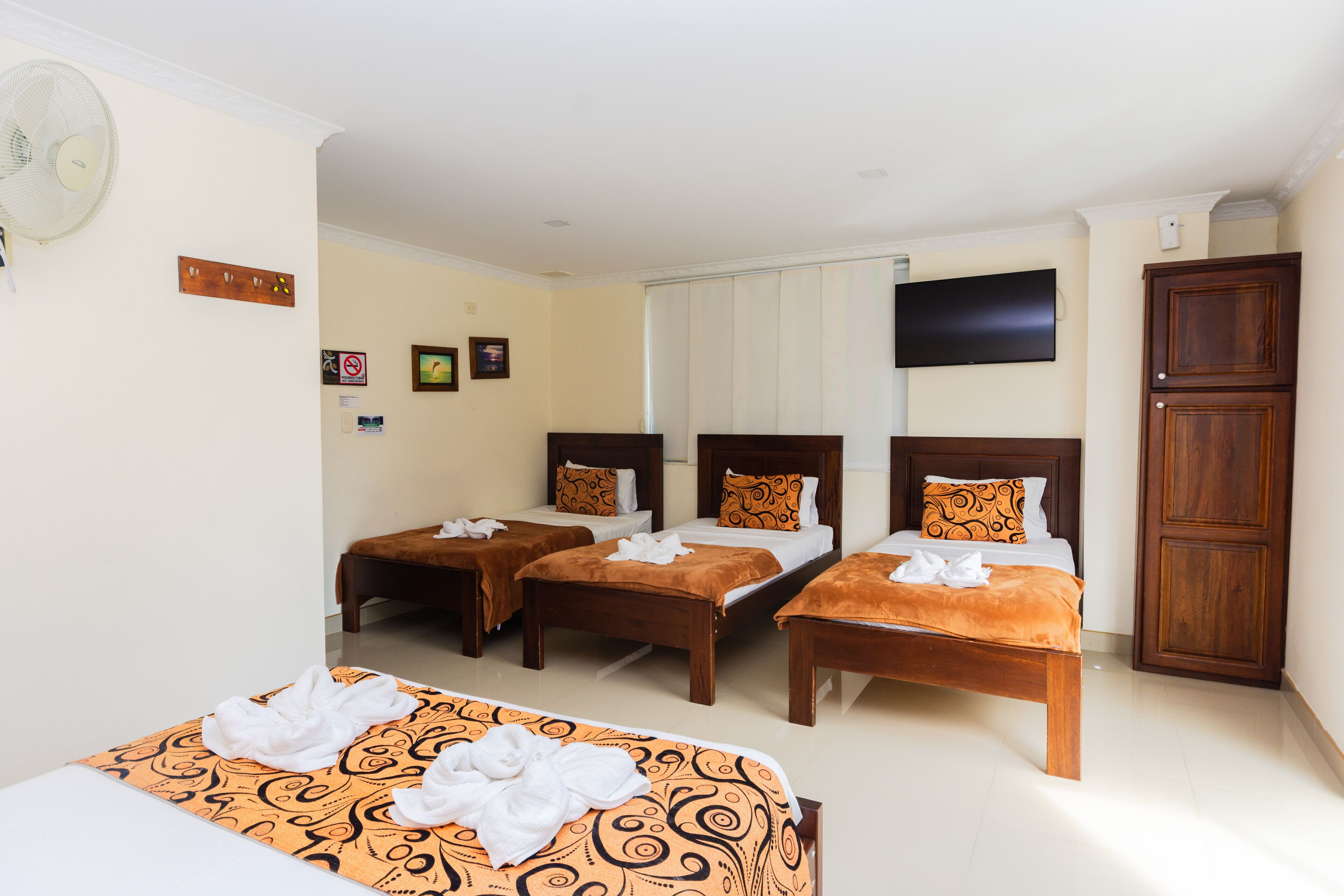 Quarto de hotel com três camas de solteiro, uma televisão grande e um guarda-roupa.