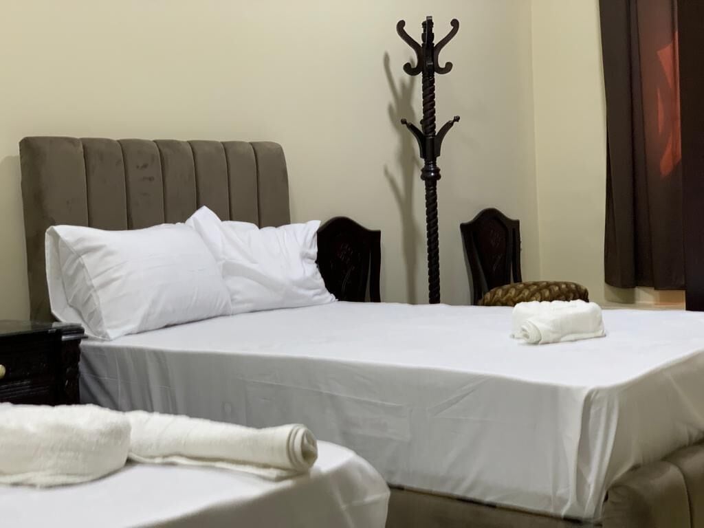 Quarto de hotel com cama, mesa de cabeceira, cabideiro e uma cadeira.