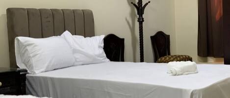 Quarto de hotel com cama, mesa de cabeceira, cabideiro e uma cadeira.