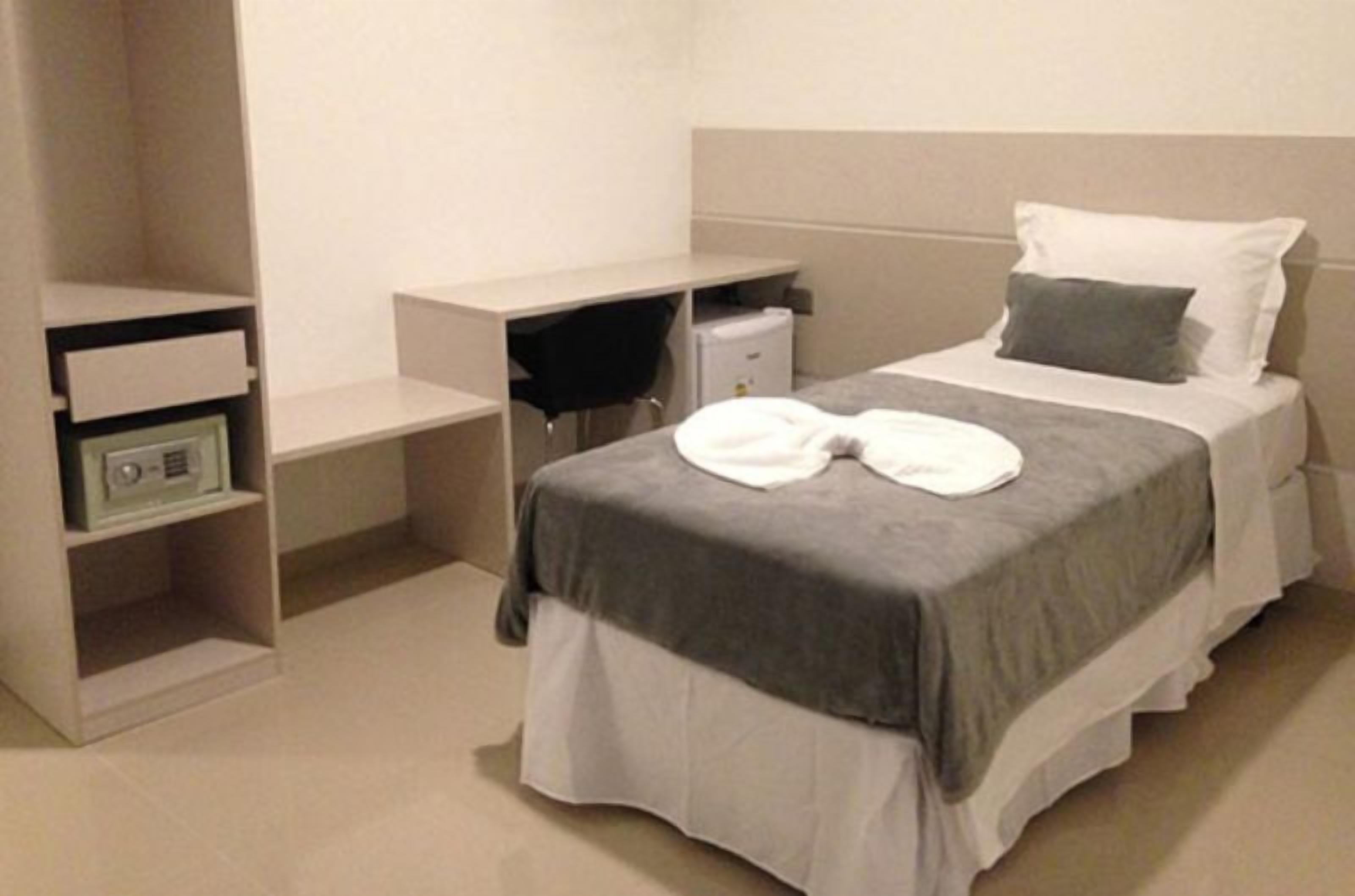 Quarto de hotel com cama, escrivaninha, cadeira e guarda-roupa.