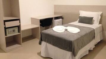 Quarto de hotel com cama, escrivaninha, cadeira e guarda-roupa.