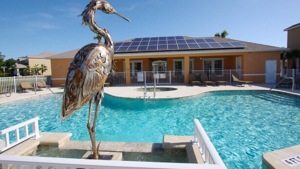 Piscina com uma escultura de pássaro, edifício com painéis solares e um céu azul límpido.