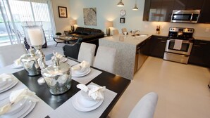 Cozinha moderna com armários escuros, eletrodomésticos de aço inoxidável e um espaço de jantar com mesa posta para quatro pessoas.